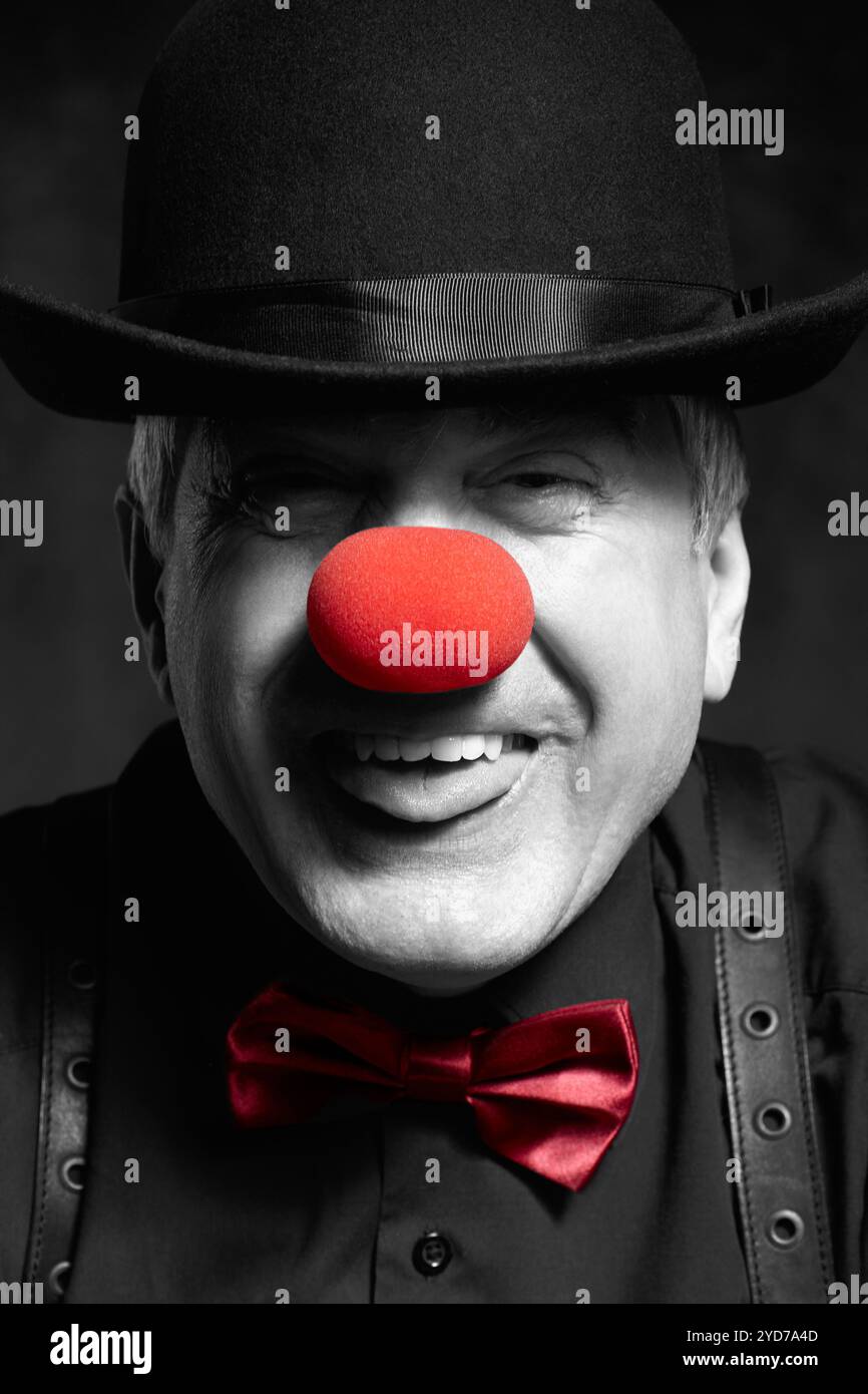 Selective color portrait of a clown with a hat pulled down over his ...