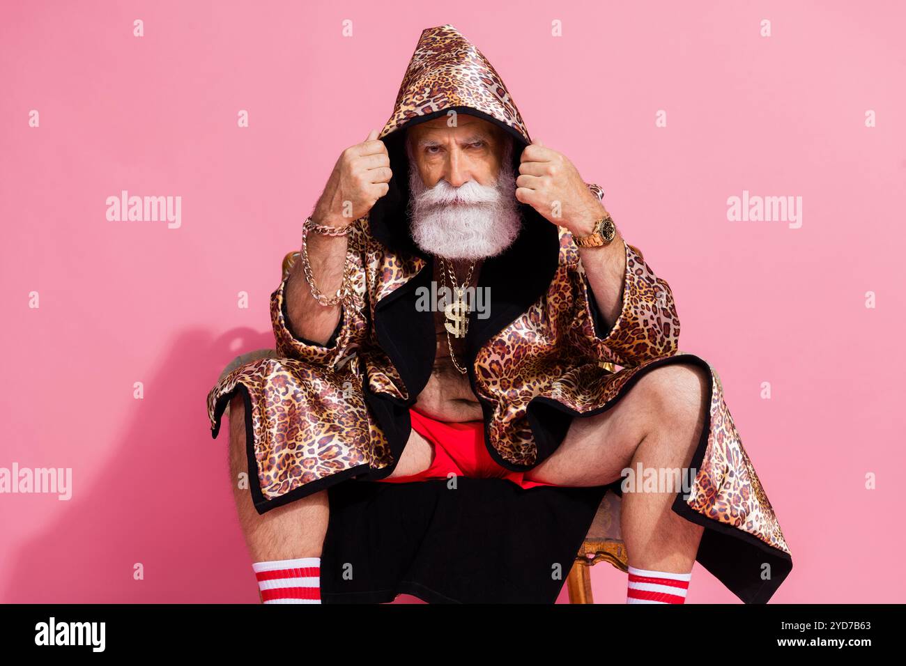 Photo of serious eccentric aged man sit chair put leopard coat hood head isolated on pink color ...