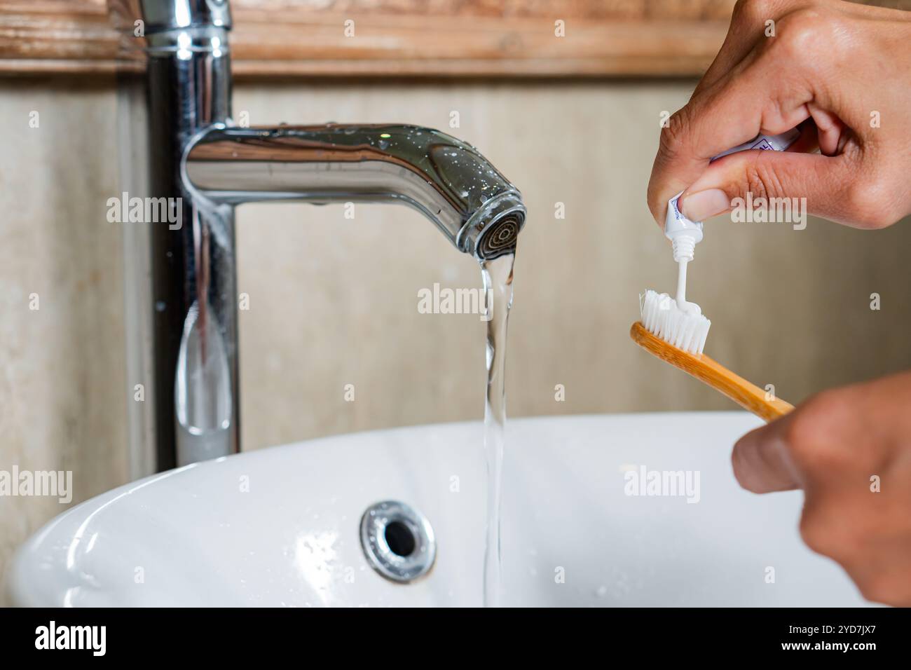 A person applying toothpaste to a bamboo toothbrush over a white sink ...