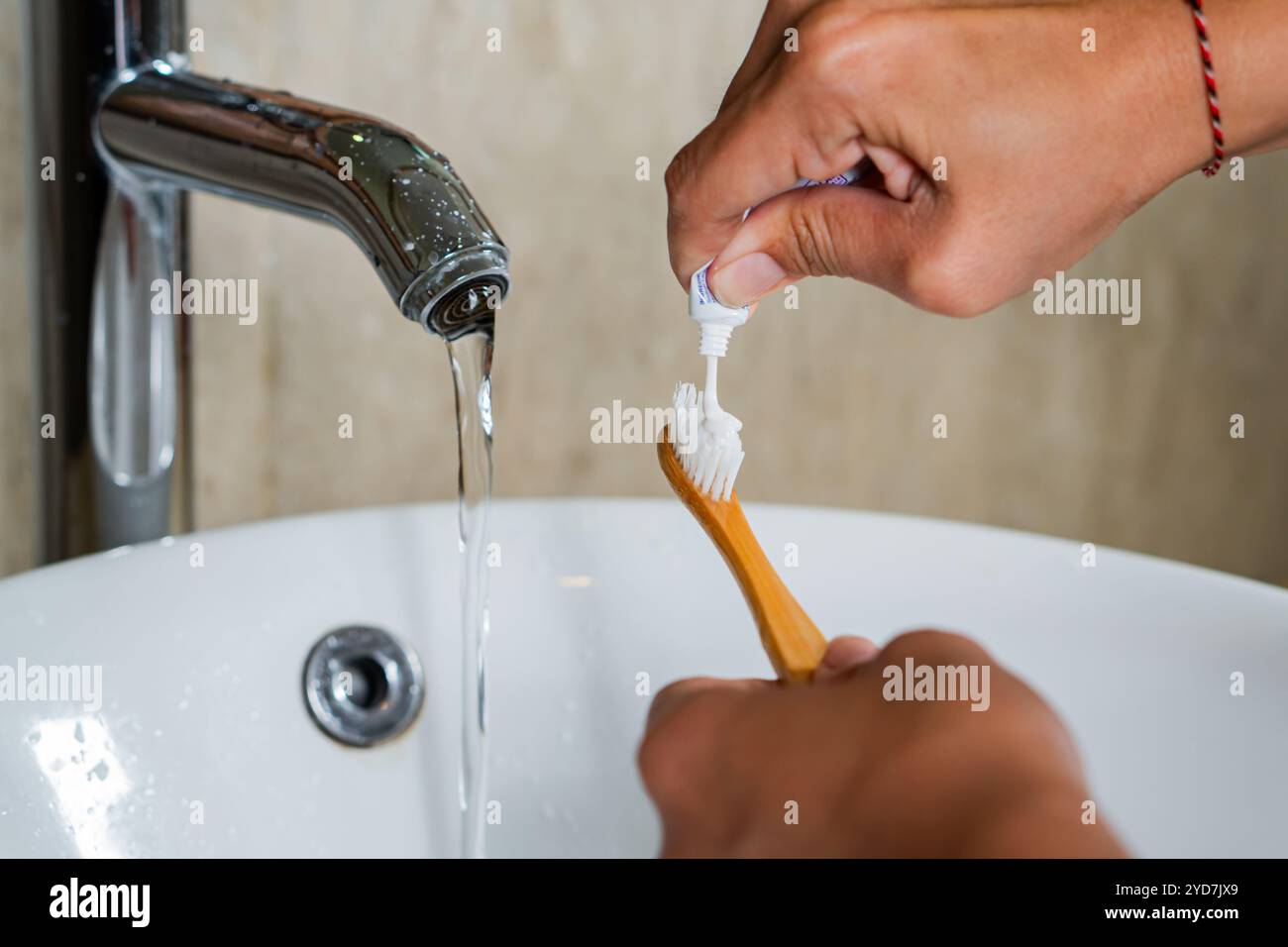 A person applying toothpaste to a bamboo toothbrush over a white sink ...