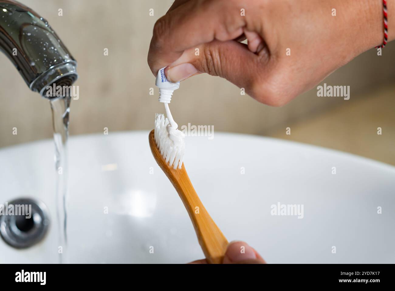 A person applying toothpaste to a bamboo toothbrush over a white sink ...