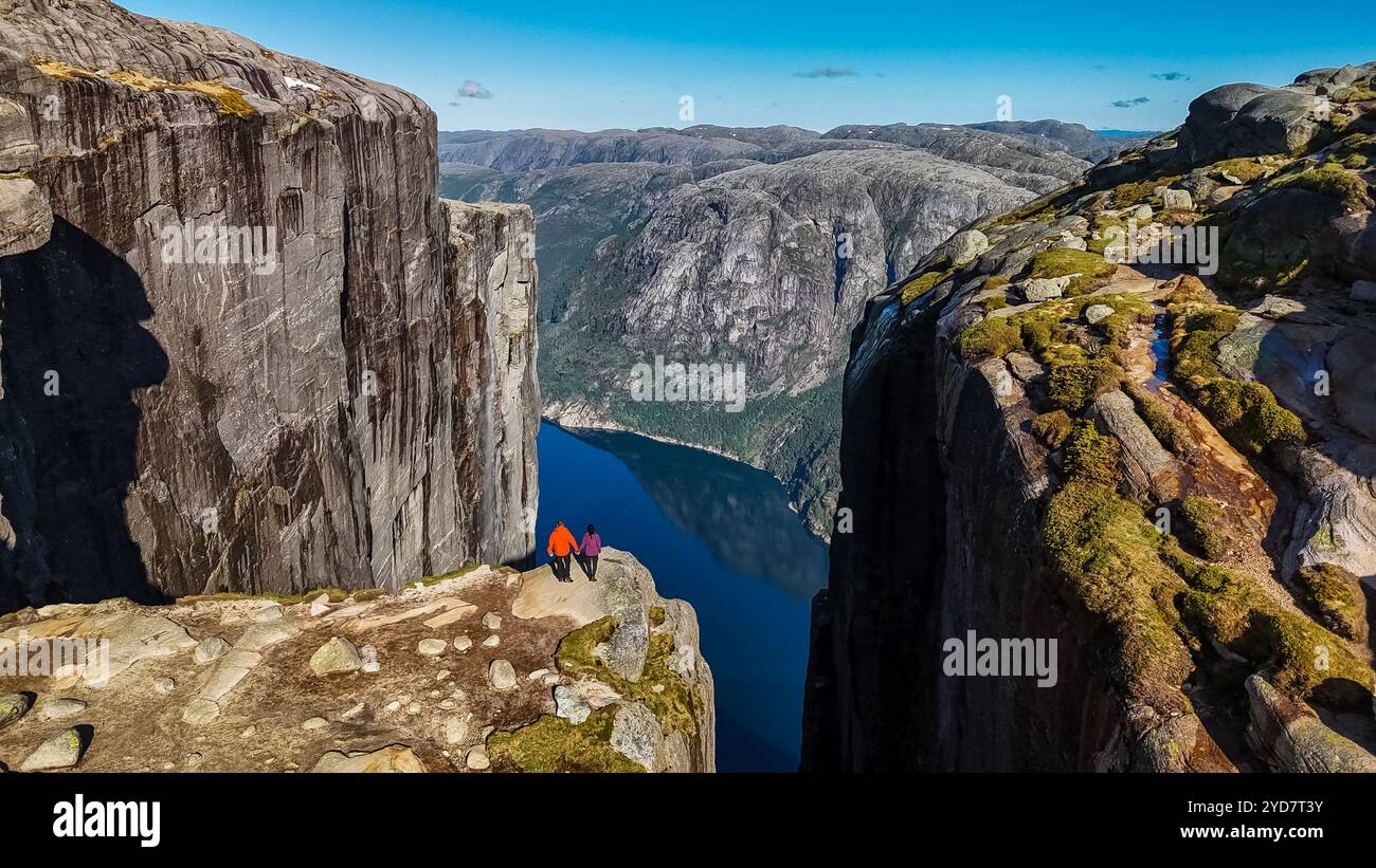 Two hikers stand on the edge of Kjeragbolten, Norway, a famous cliff in ...