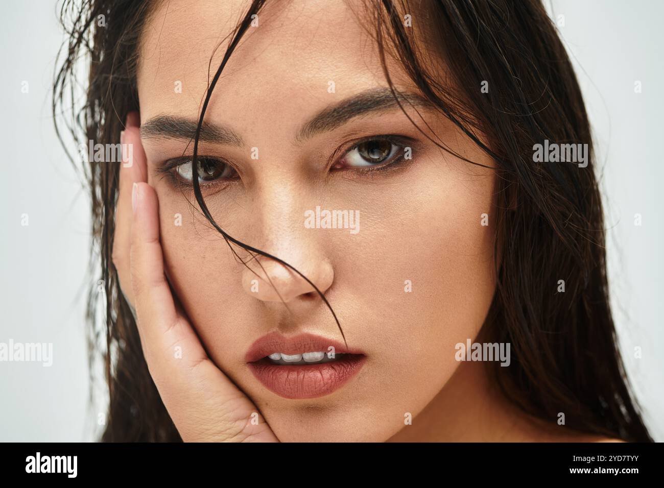 A beautiful woman gazes intensely while softly touching her face ...