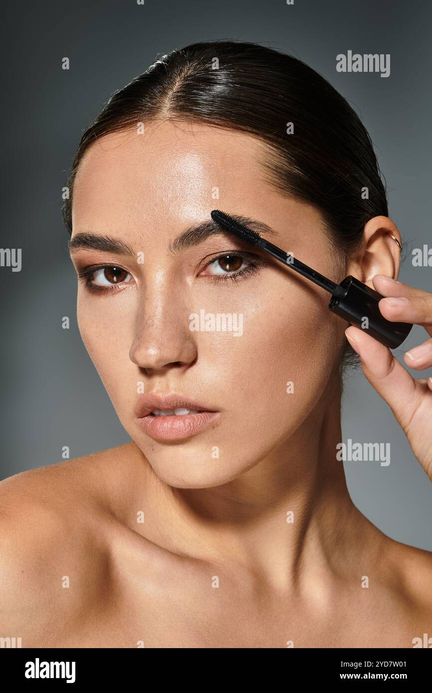 A beautiful woman focuses intently while applying brow gel to her ...