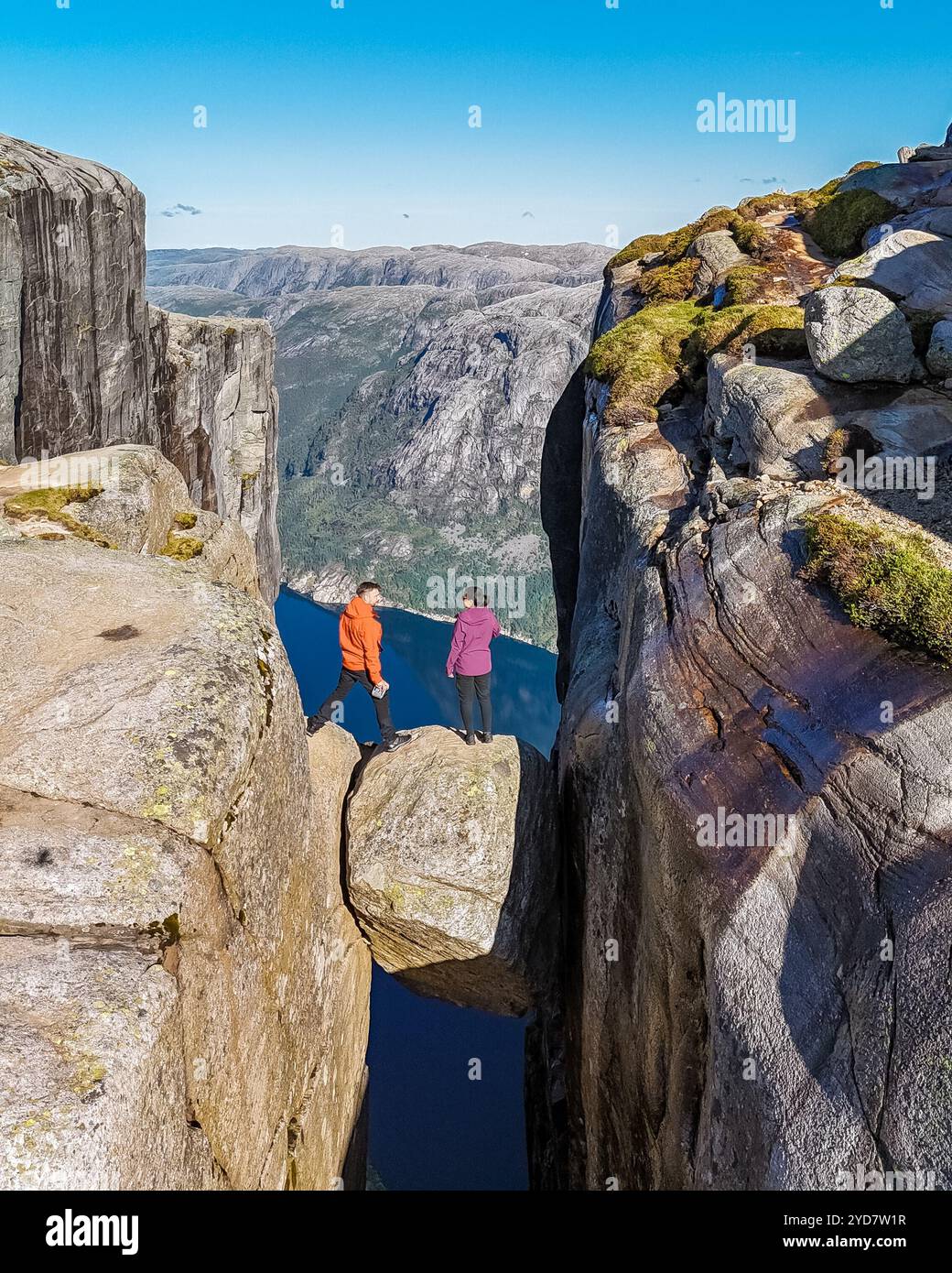 Two people stand on the edge of Kjeragbolten Pulpit Rock in Norway ...