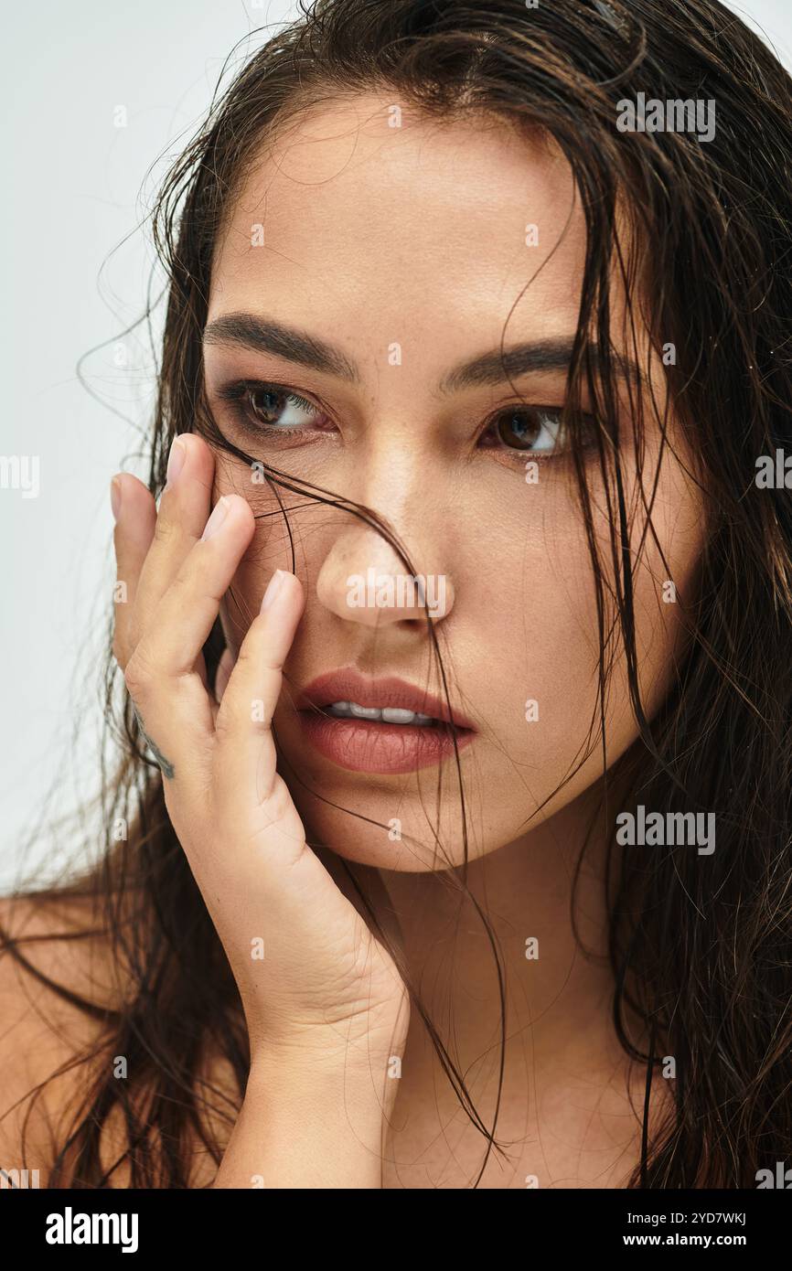 A lovely woman with wet hair brushes her fingers against her face ...