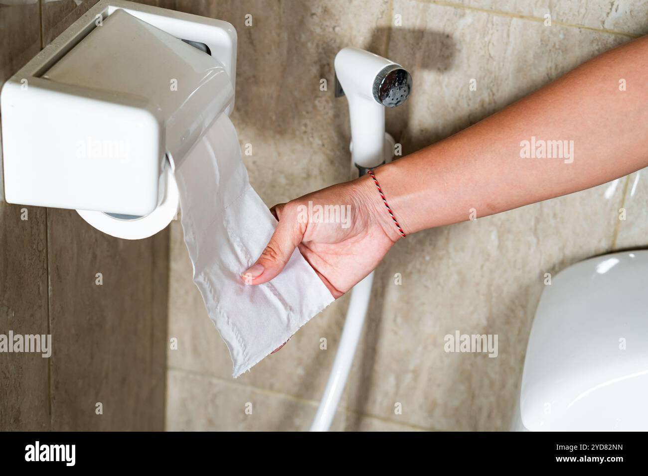 A hand reaching for toilet paper from a holder in a bathroom. The ...