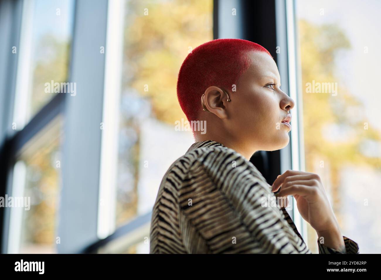 A bald woman with striking red hair looks pensively outside, reflecting ...