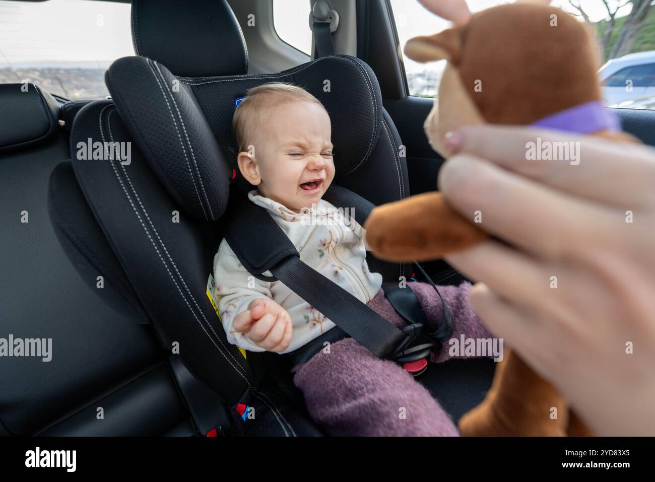 Mother trying to entertain crying baby in car seat with a toy Stock ...