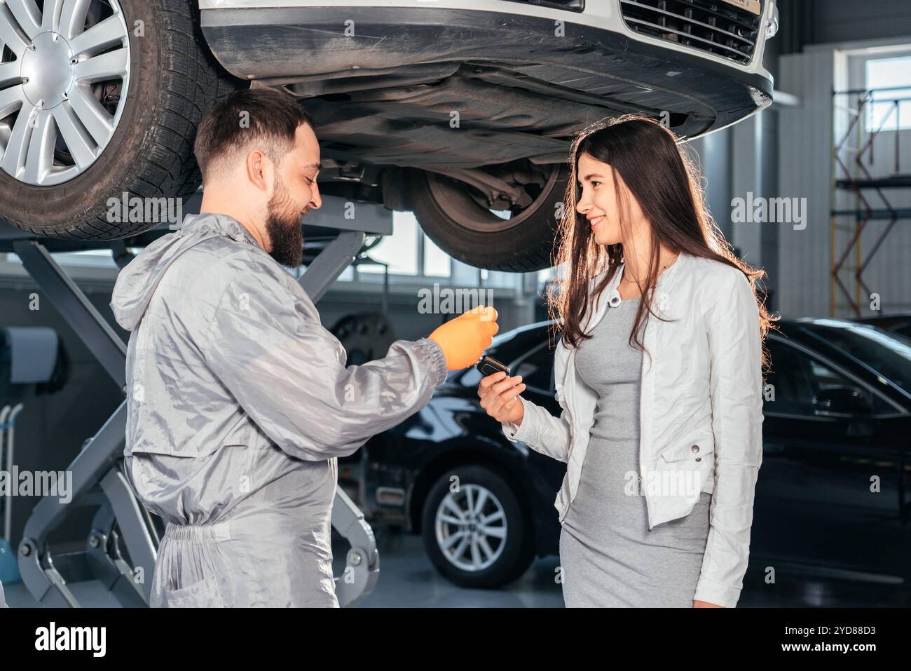Auto Mechanic giving the car keys to his female customer in workshop at ...