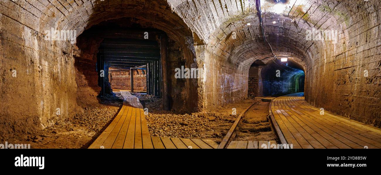 Old underground mine tunnel with wooden walkways and arched stone walls ...