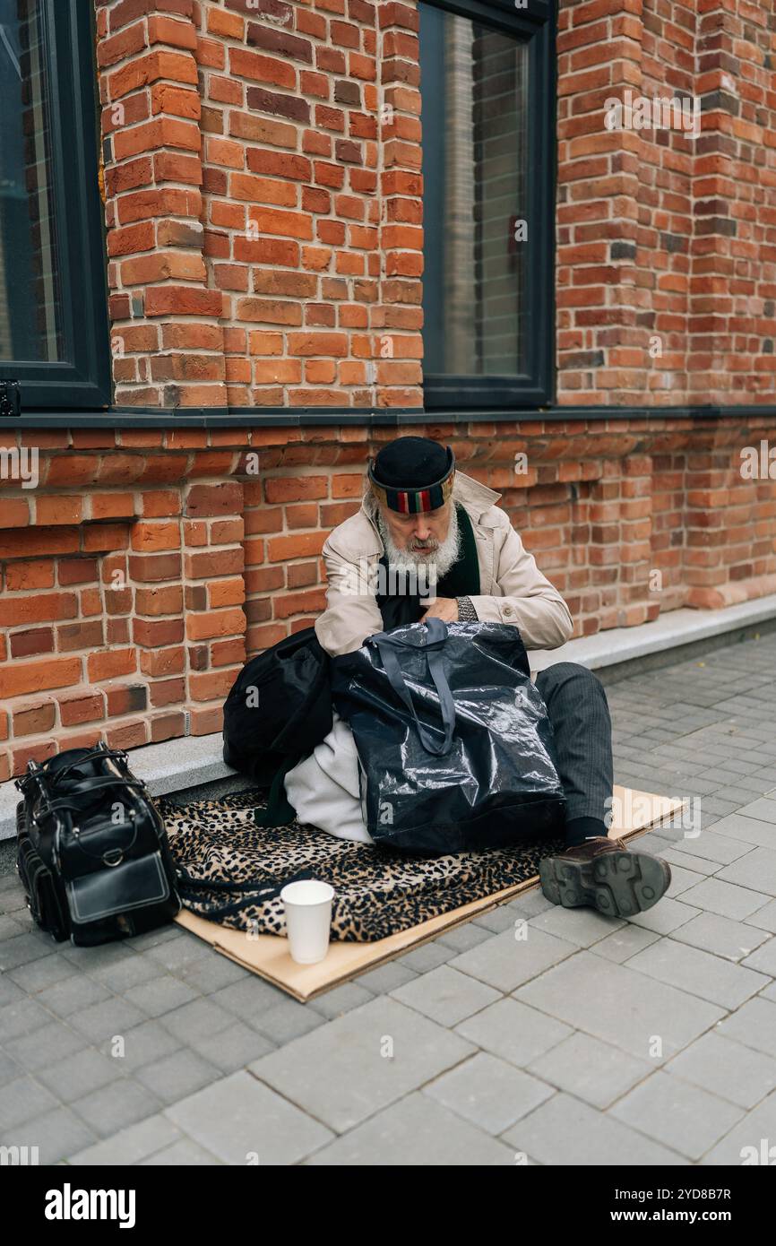 Full length vertical portrait of homeless elderly man sitting on urban ...