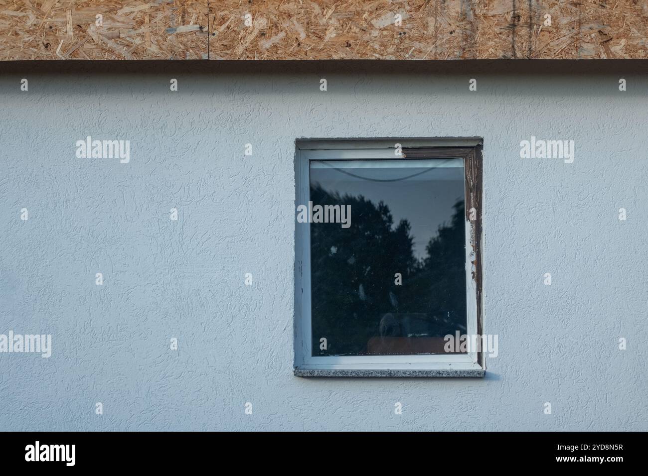 Small square window is reflecting trees on a gray plastered wall with ...