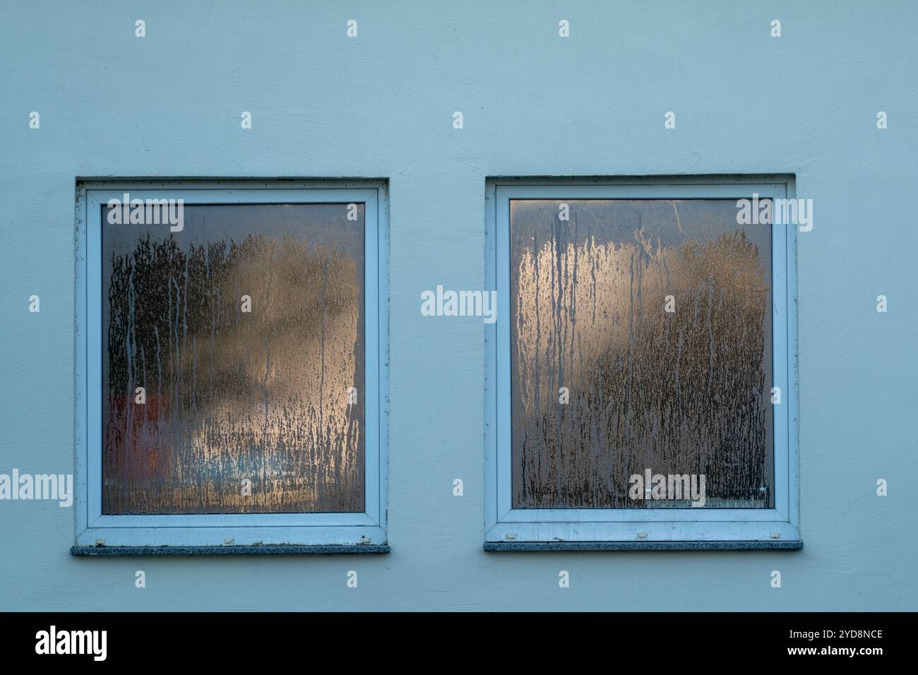 Condensation forming on two windows of a building with a pale blue wall ...