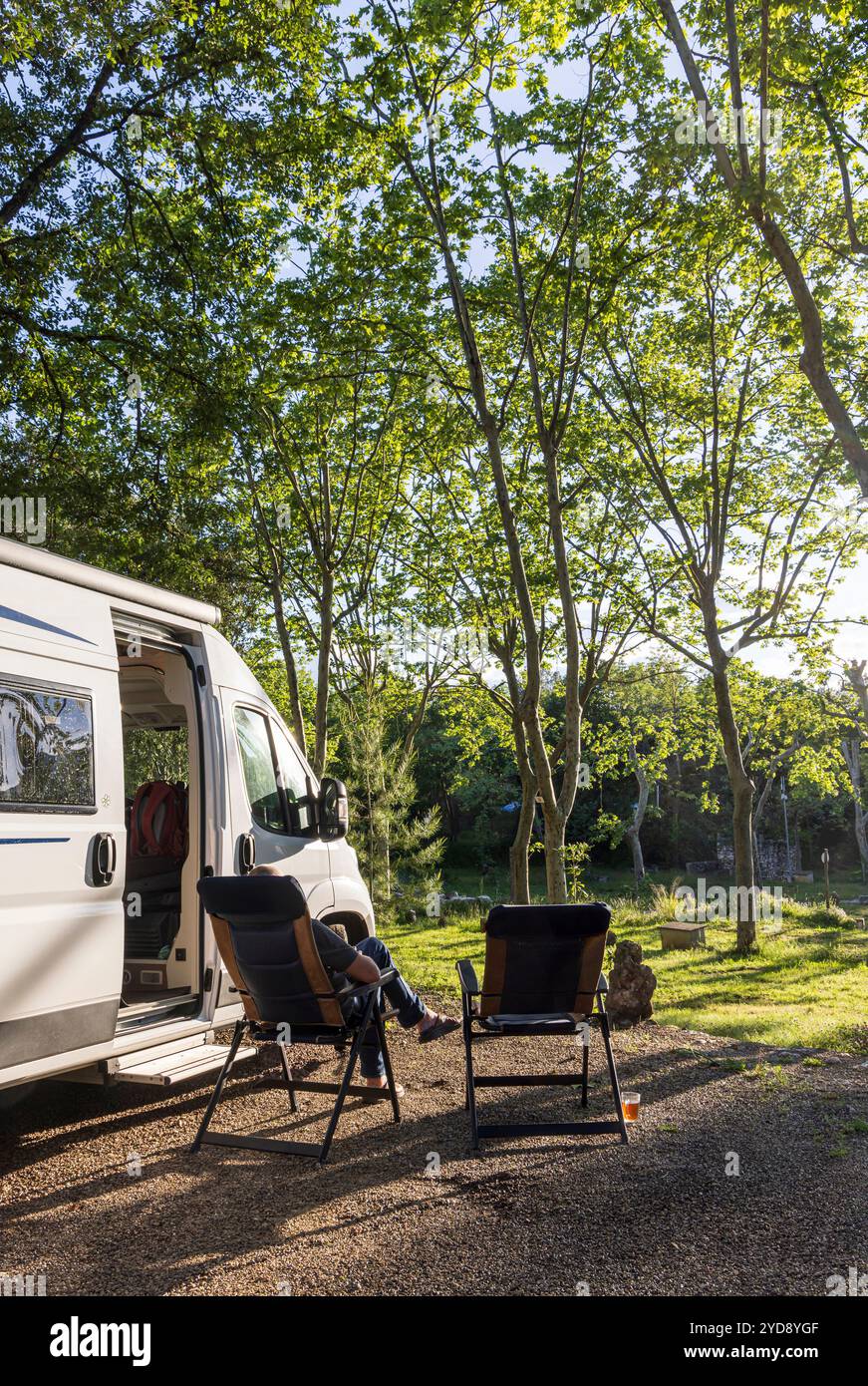Relaxing in a chair in the sun beside camper at campsite with a lot of ...