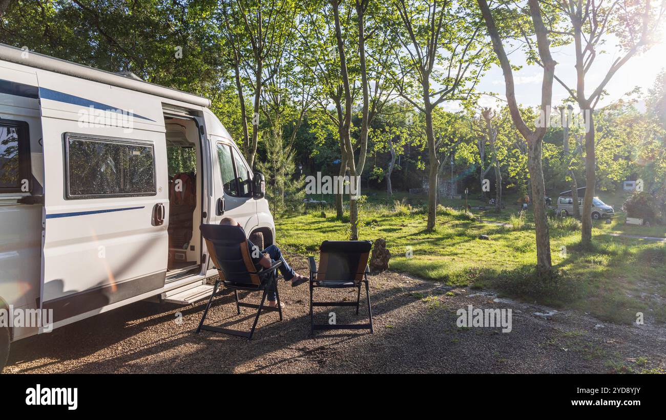 Relaxing in a chair in the sun beside camper at campsite with a lot of ...