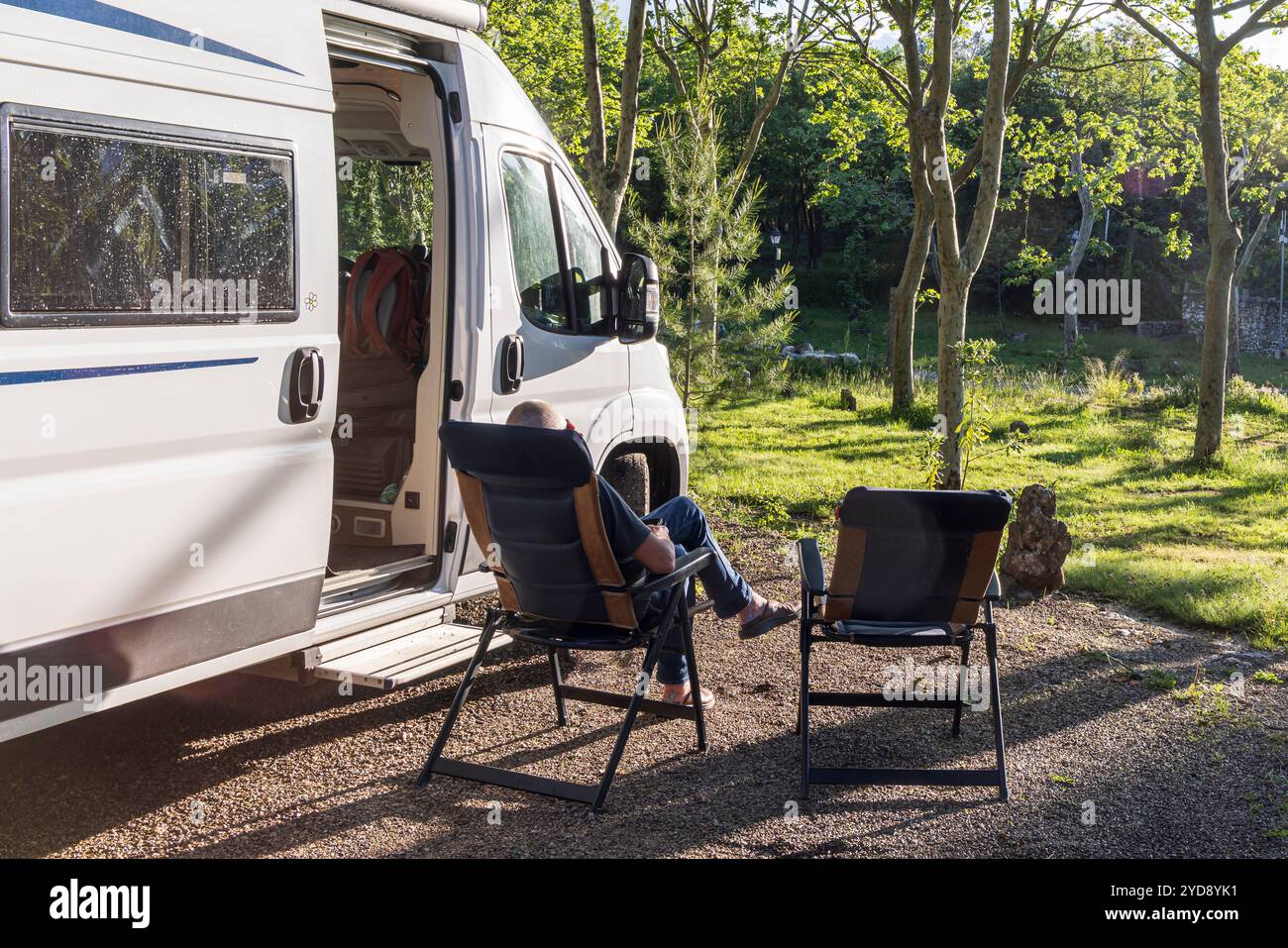 Relaxing in a chair in the sun beside camper at campsite with a lot of ...