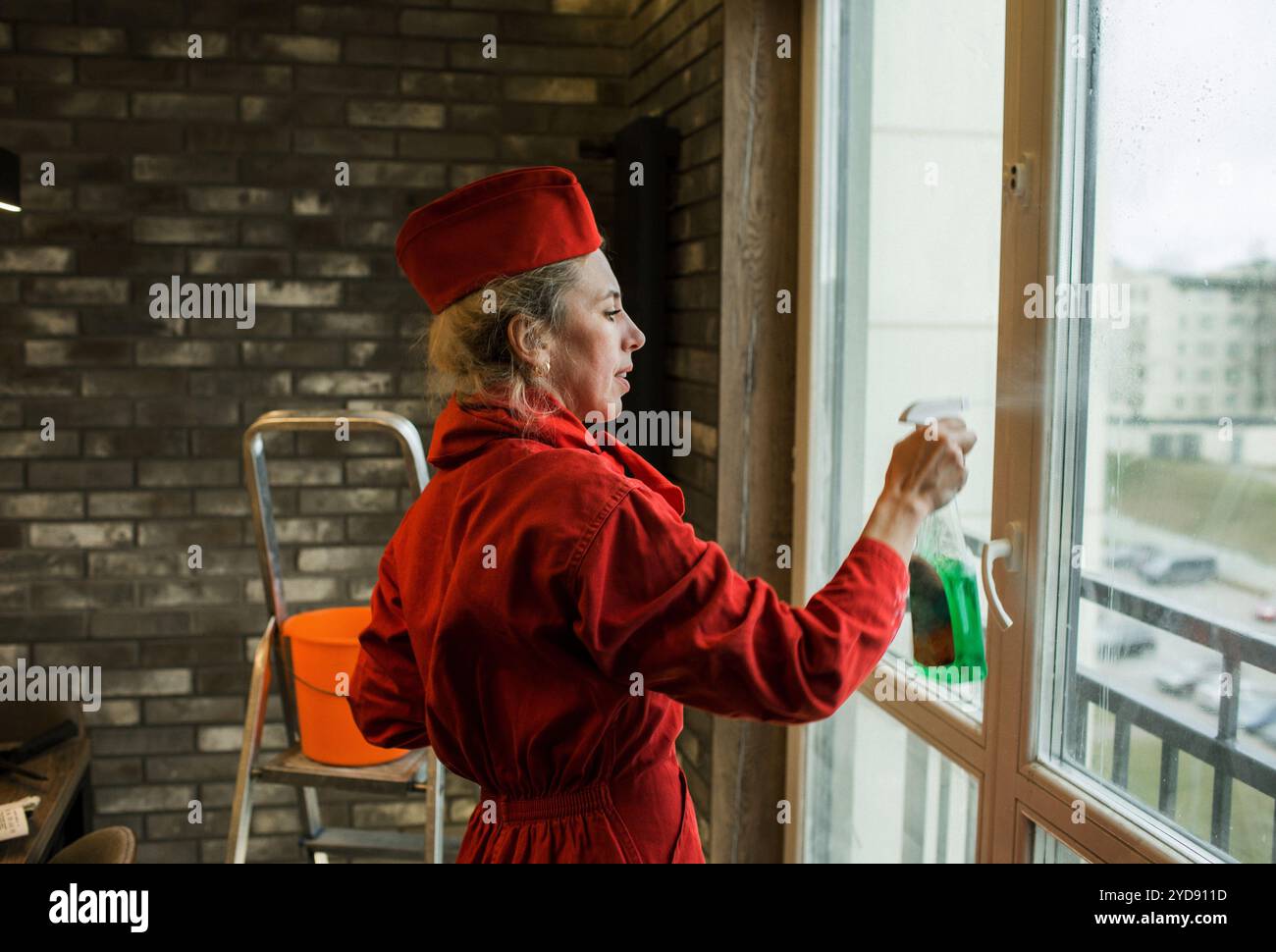 A woman in a red jumpsuit is cleaning a window with a spray bottle and ...