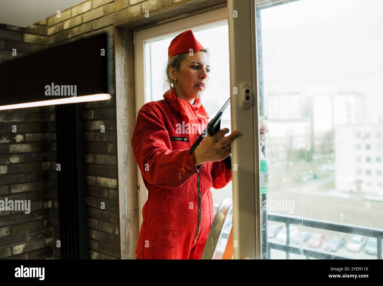 A woman in a red jumpsuit is cleaning a window with a squeegee and ...
