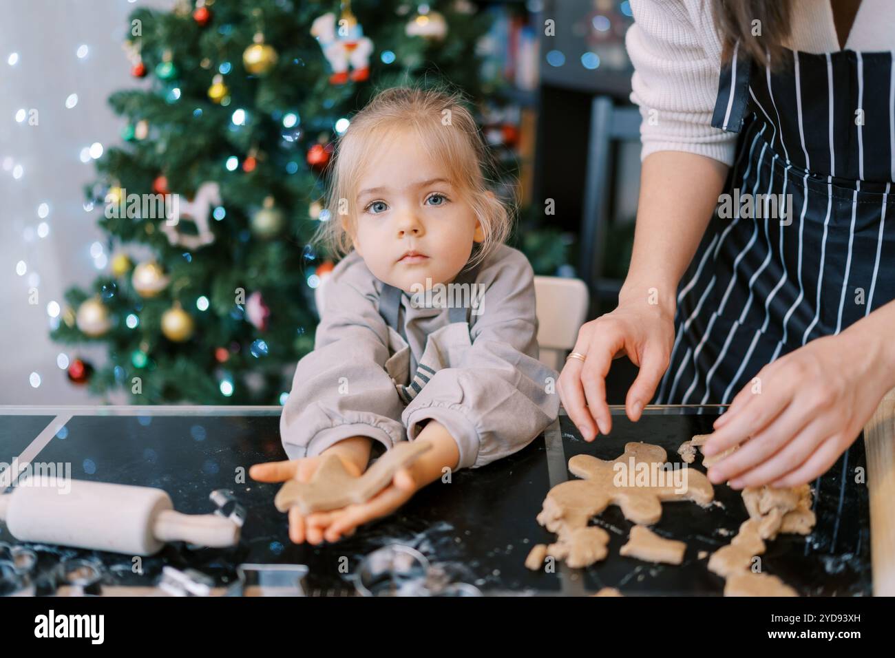 Little girl holds a cut out cookie on her outstretched palm while ...