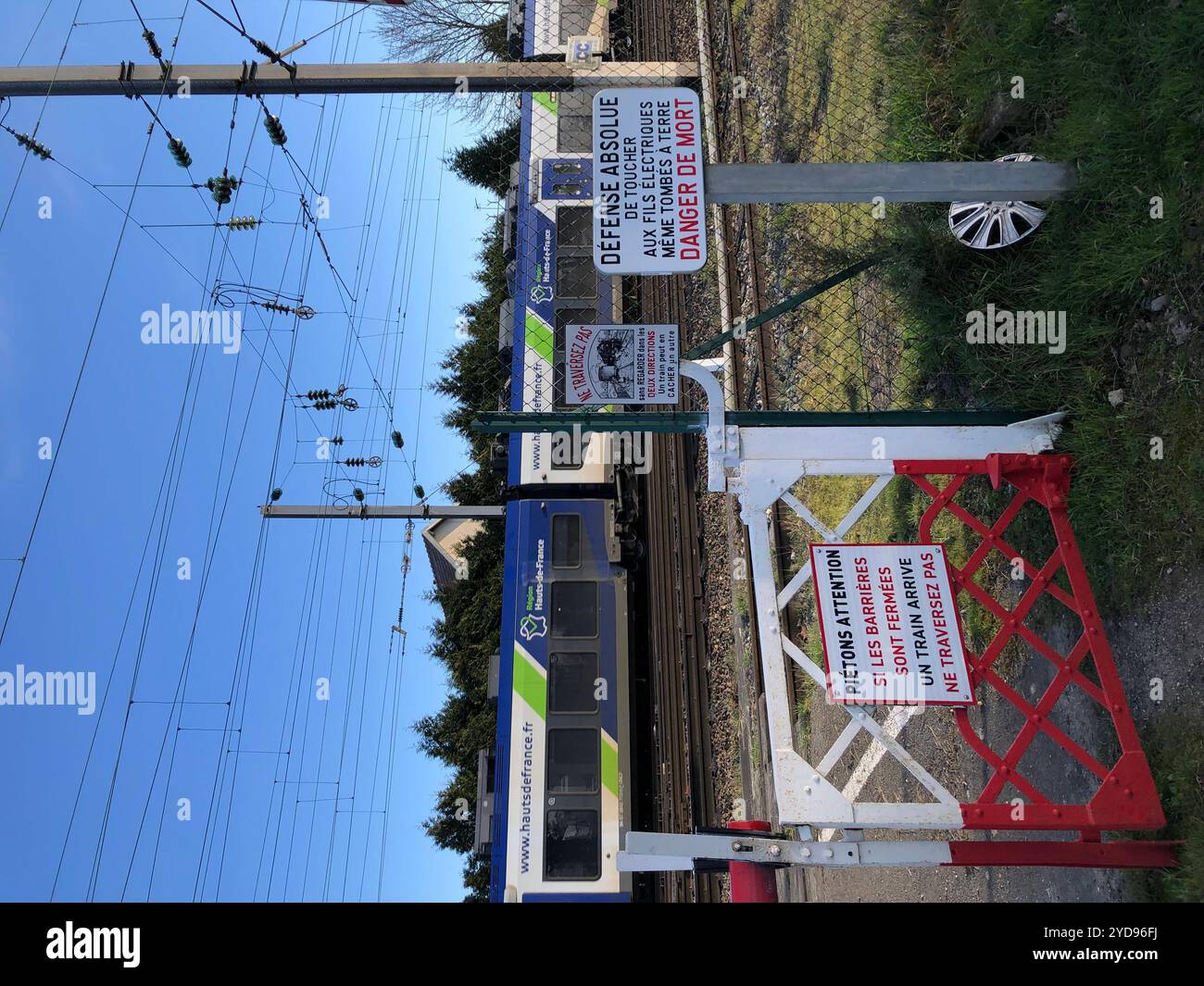 A railway crossing with a barrier and warning signs. Train approaches a ...