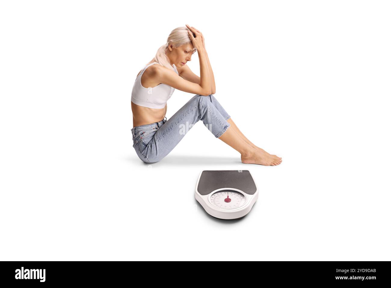 Scared skinny woman sitting on the ground and looking at a weight scale ...