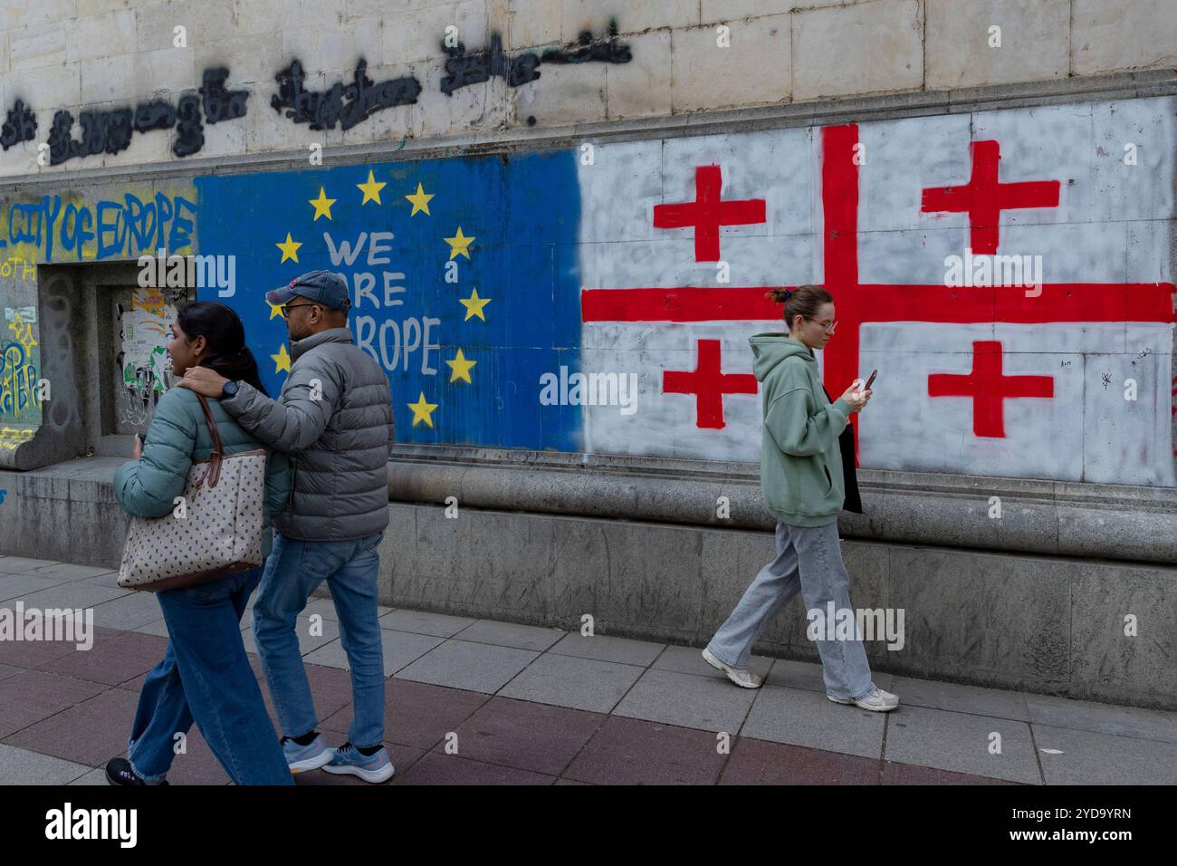 A couple, arm in arm, walk past the EU and Georgian flag mural, while a ...