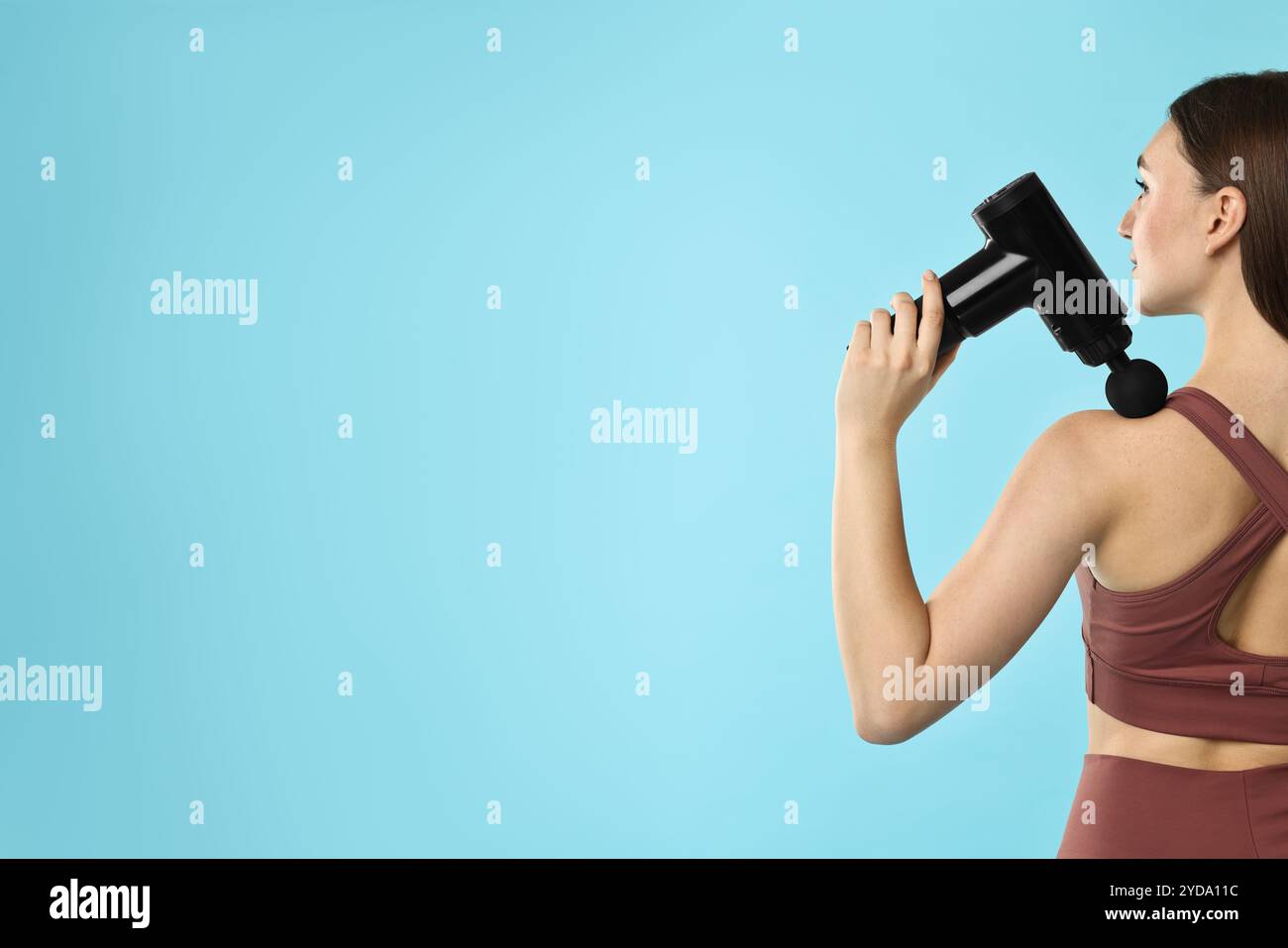 Woman using percussive massager to relieve trapezius muscle on light ...