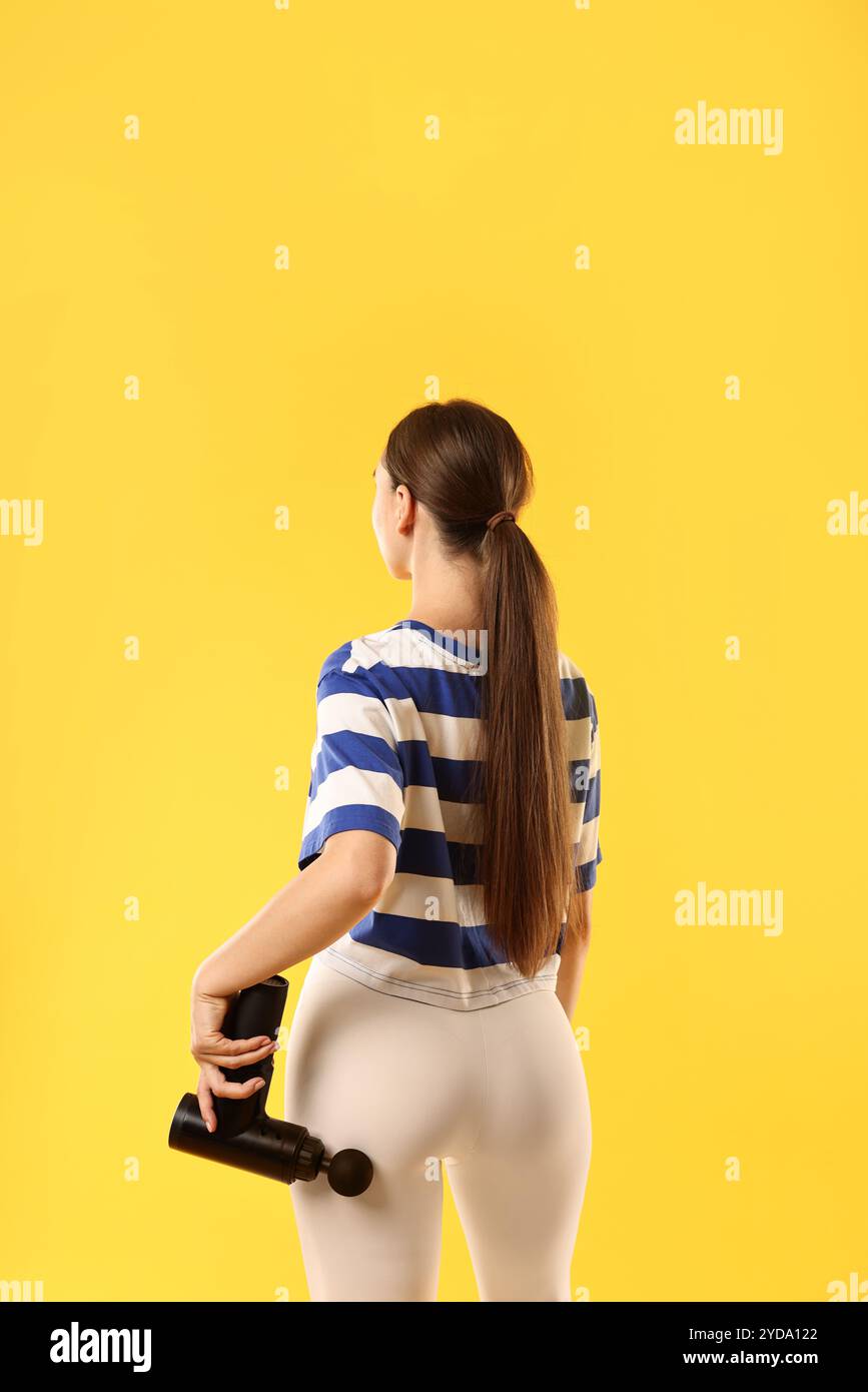 Woman using percussive massager to relax buttock muscles on yellow ...