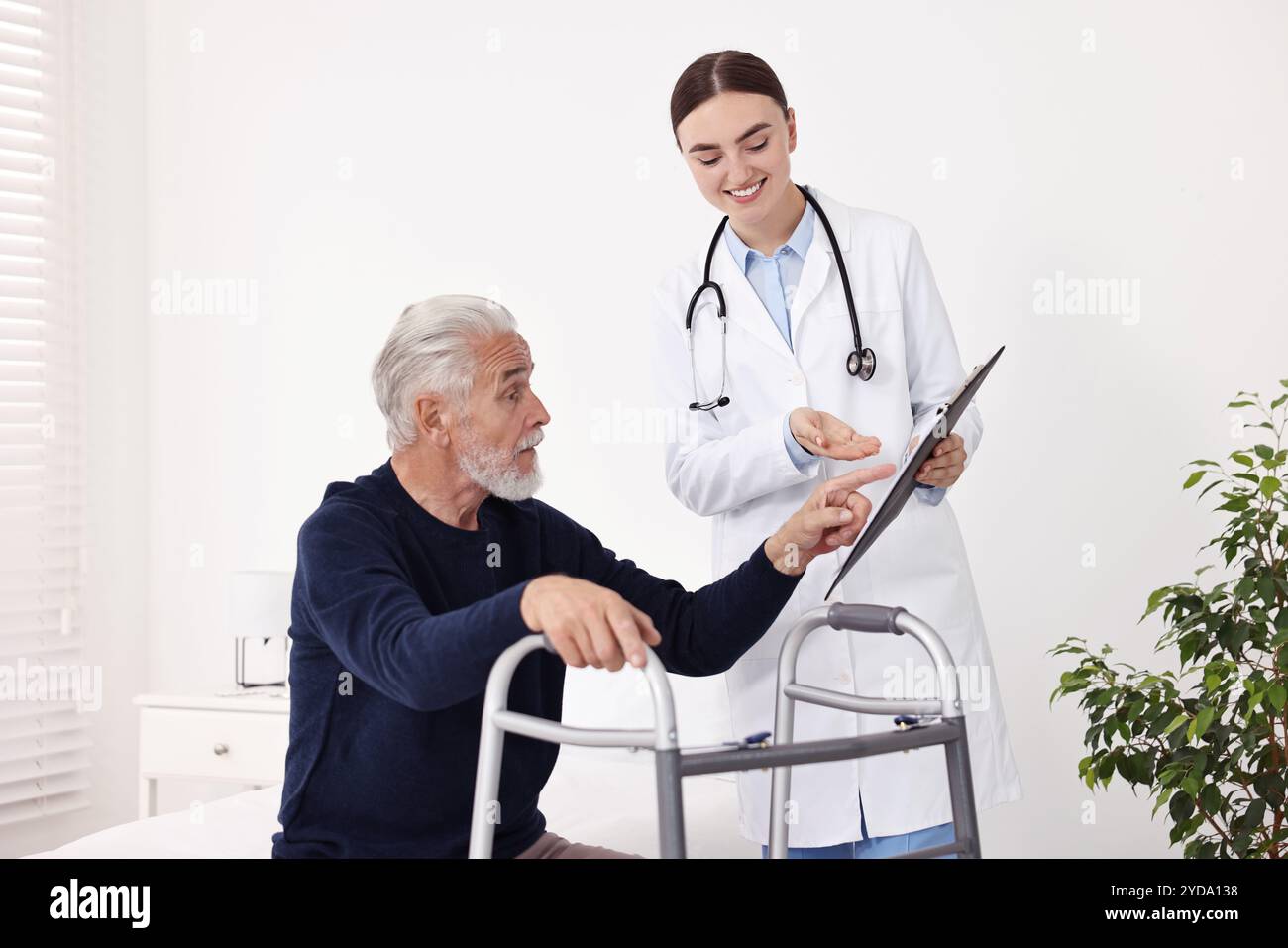 Doctor consulting senior patient with walking frame in hospital ward ...