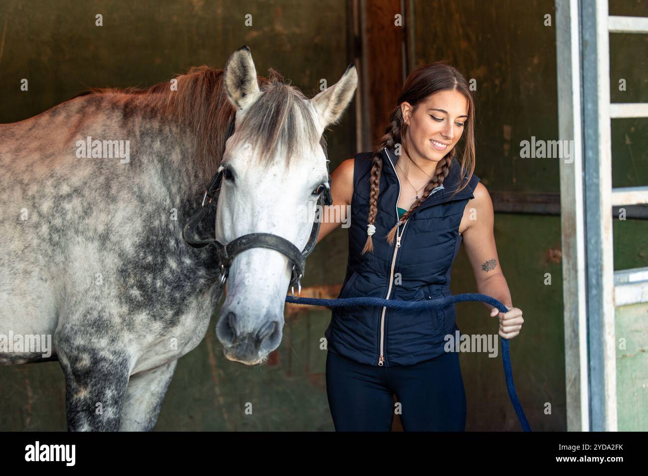 cheerful woman rider stands in the stable, smiling as she grips the ...