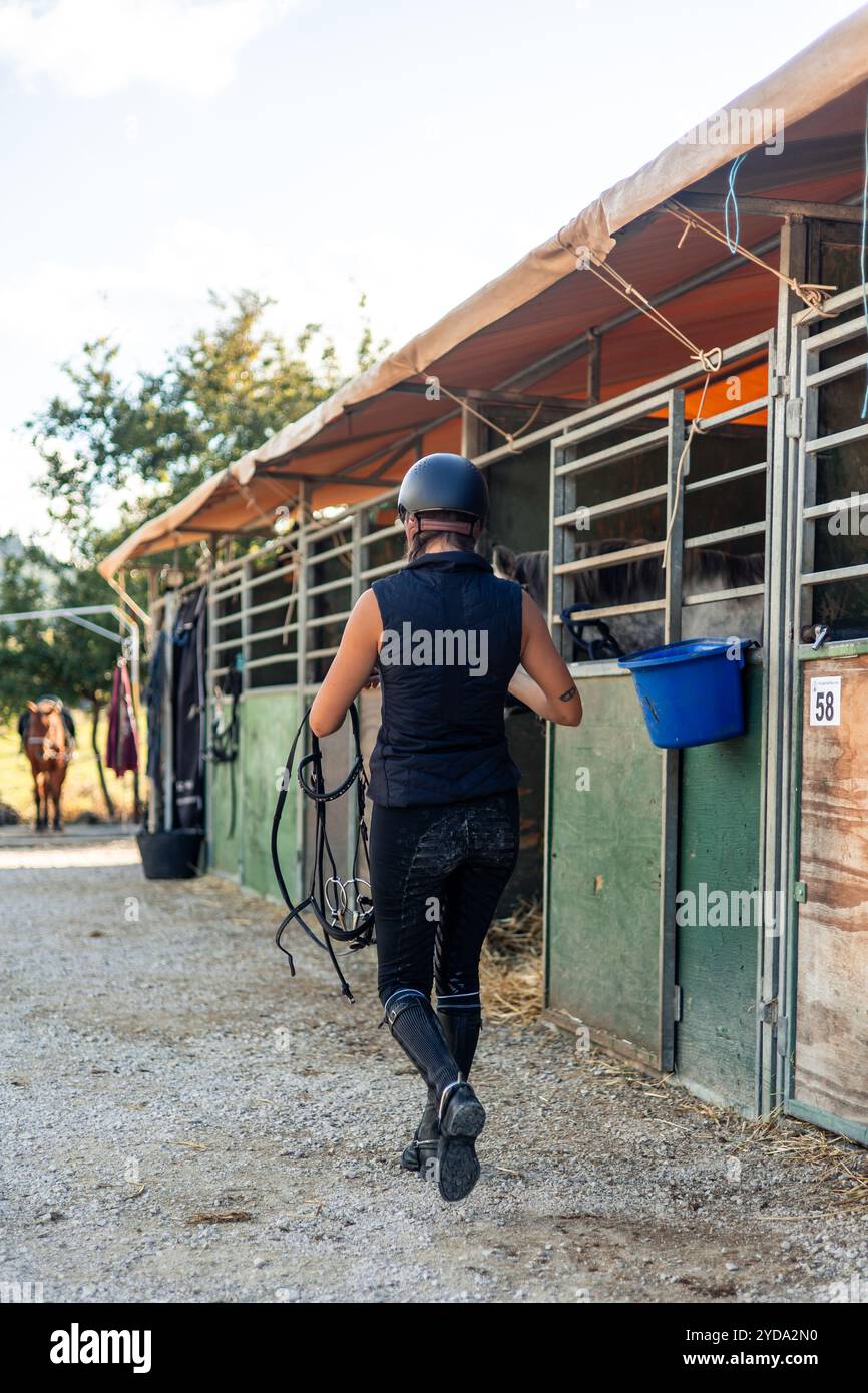 vertical female rider, seen from behind, strolls through the ranch ...