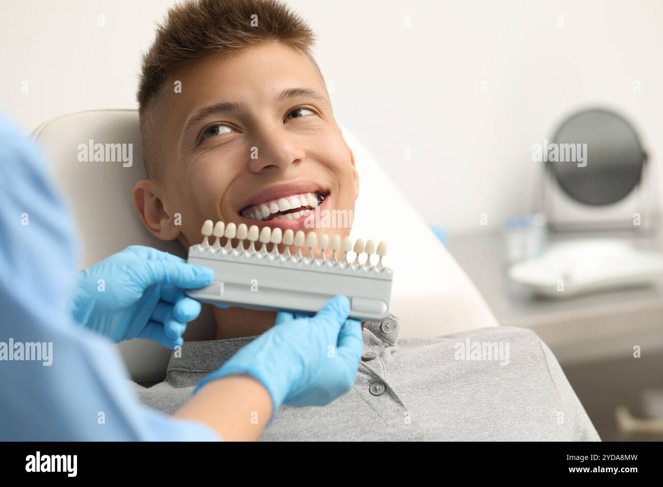 Doctor checking young man's teeth color in clinic, closeup. Dental ...