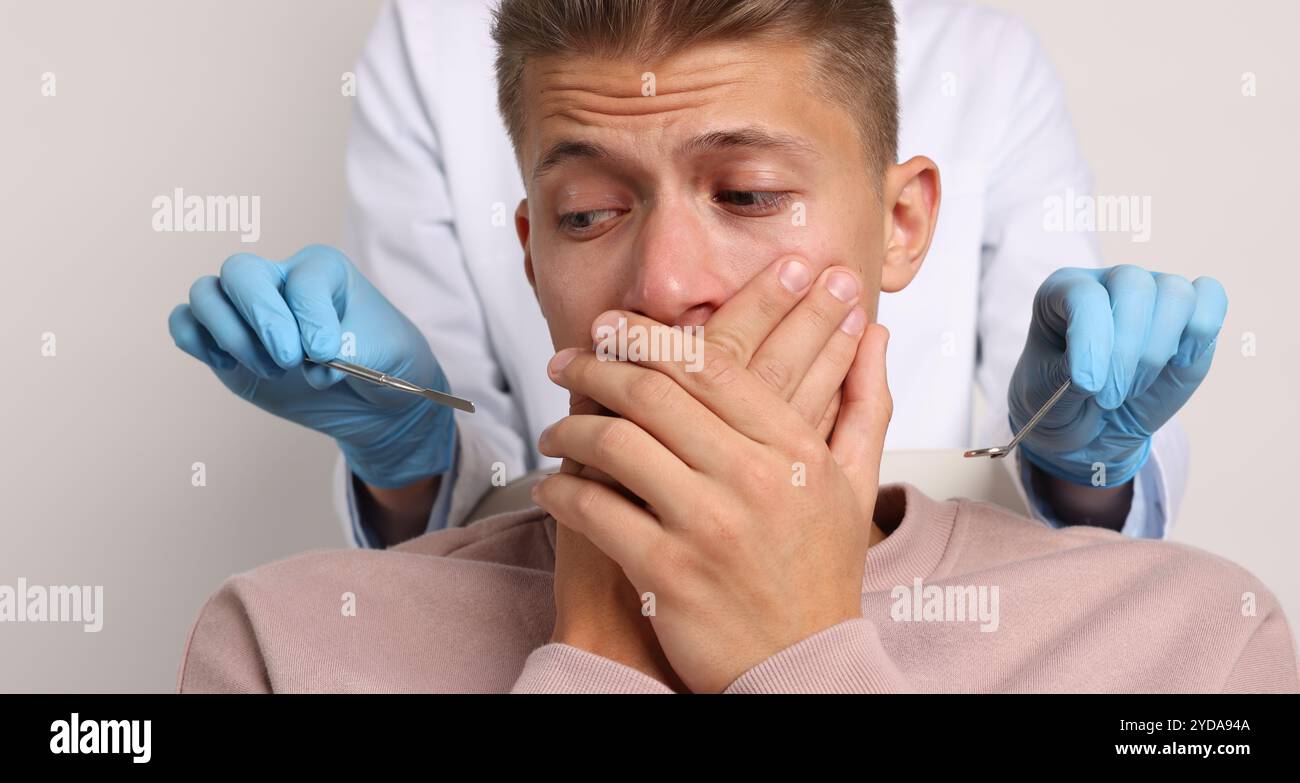 Dental phobia. Dentist working with scared man on light grey background ...