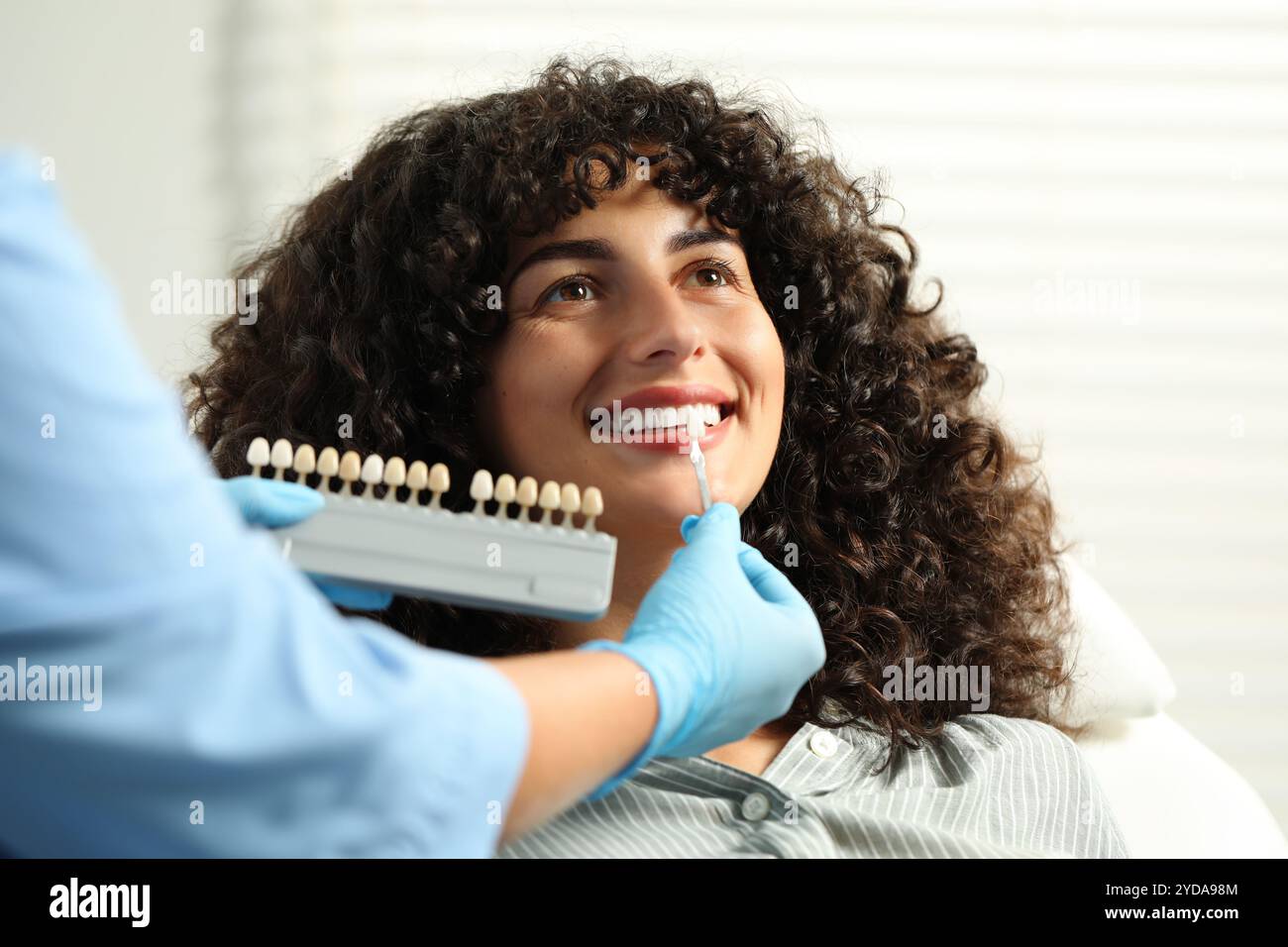 Doctor checking young woman's teeth color in clinic, closeup. Dental ...
