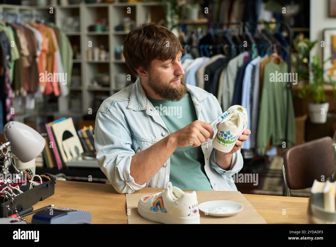 Bearded male worker of thrift shop upcycling secondhand cross shoes ...