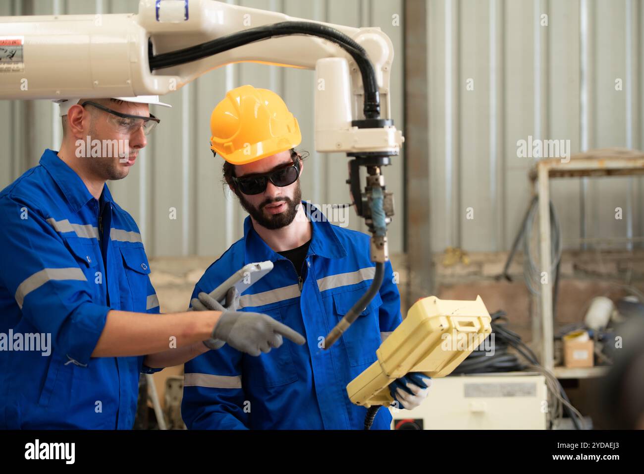 Both of engineers are manipulating a welding robot hand. By combining ...