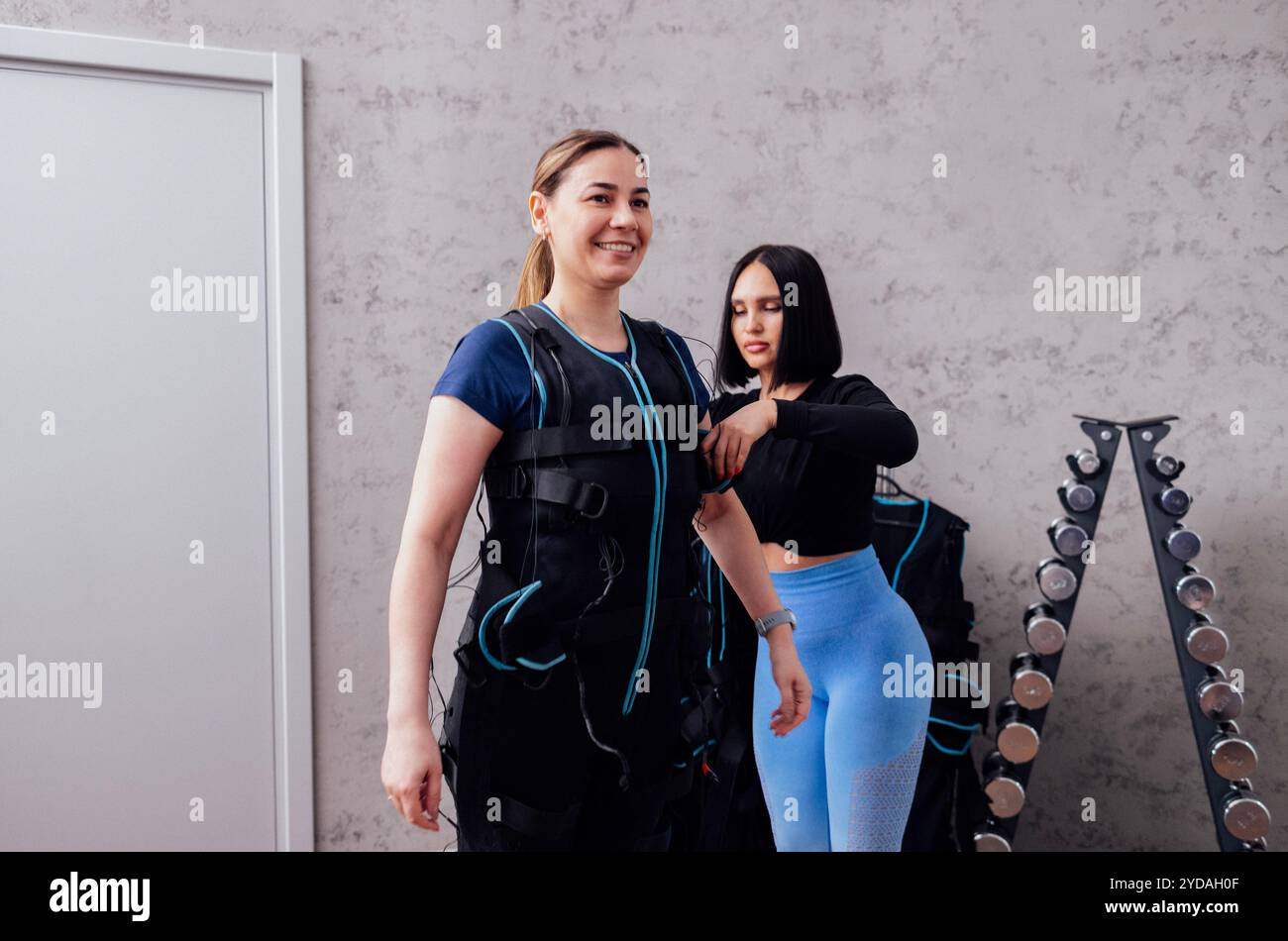 Female coach puts on suit for ems workout on smiling young woman. The ...