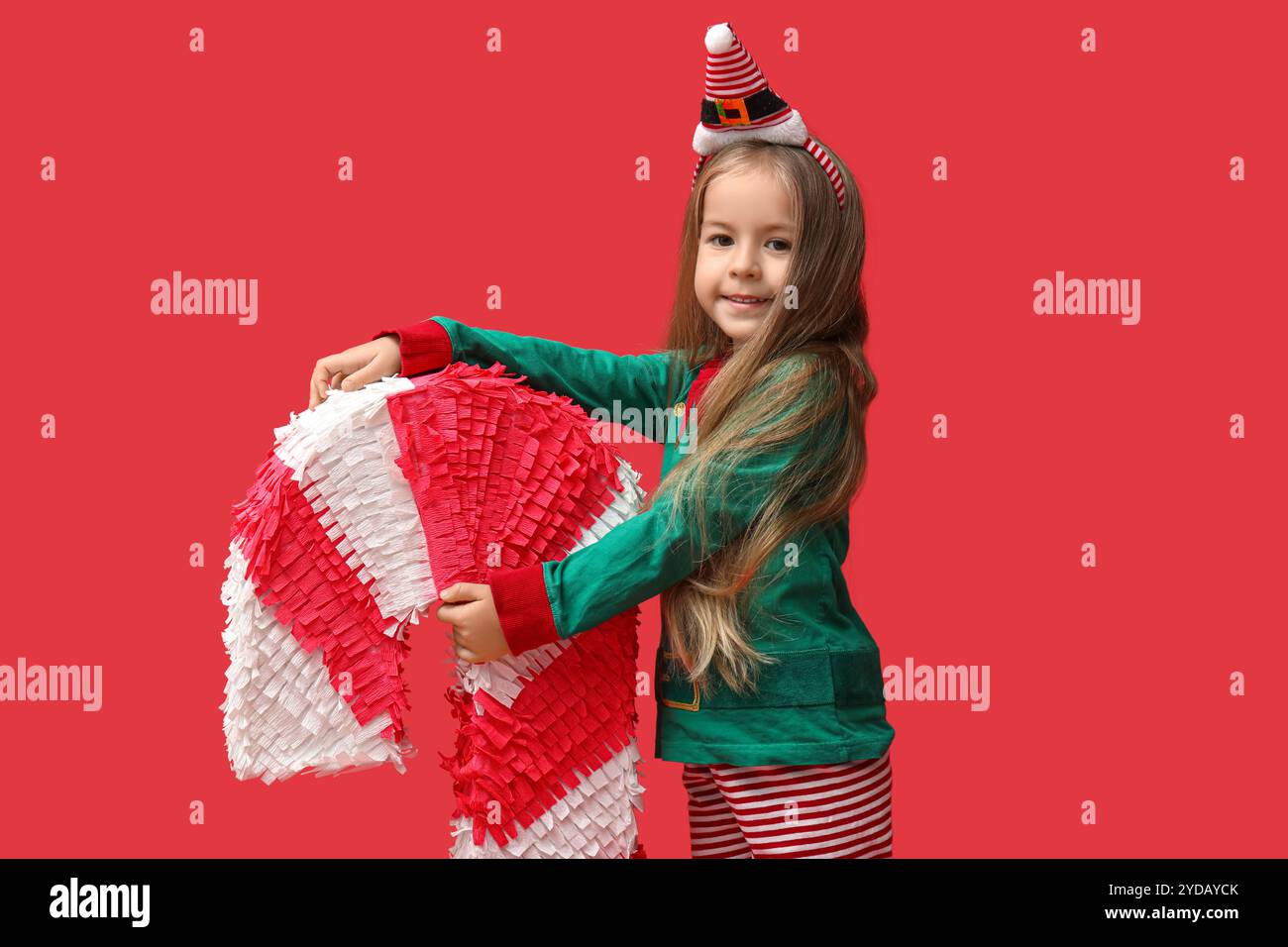 Cute little girl in Christmas elf costume with candy cane pinata on red ...