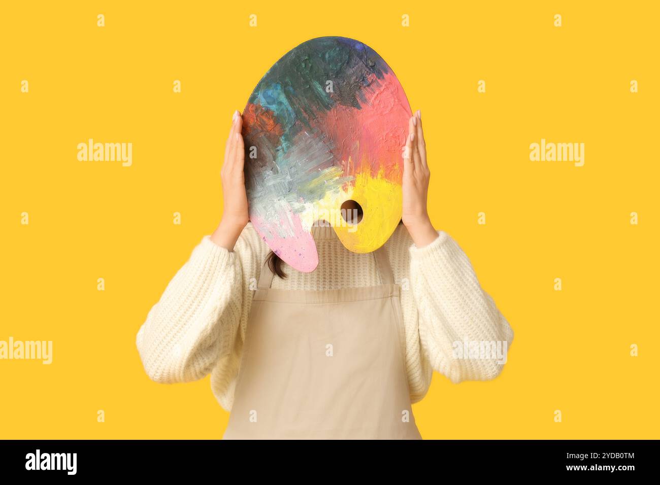 Female artist hiding face behind palette on yellow background Stock ...