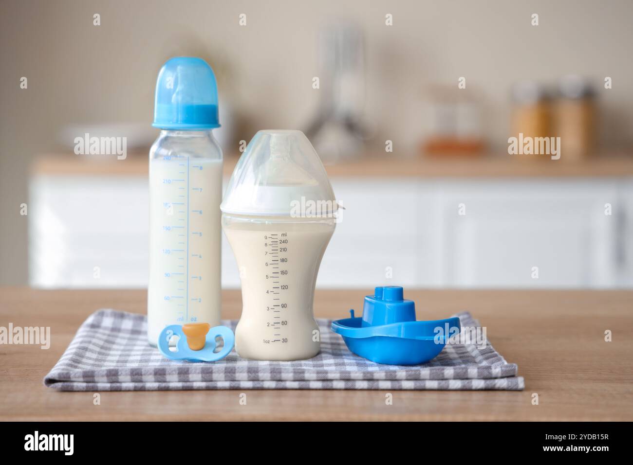 Bottles of baby milk formula, pacifier and toy boat on wooden kitchen ...