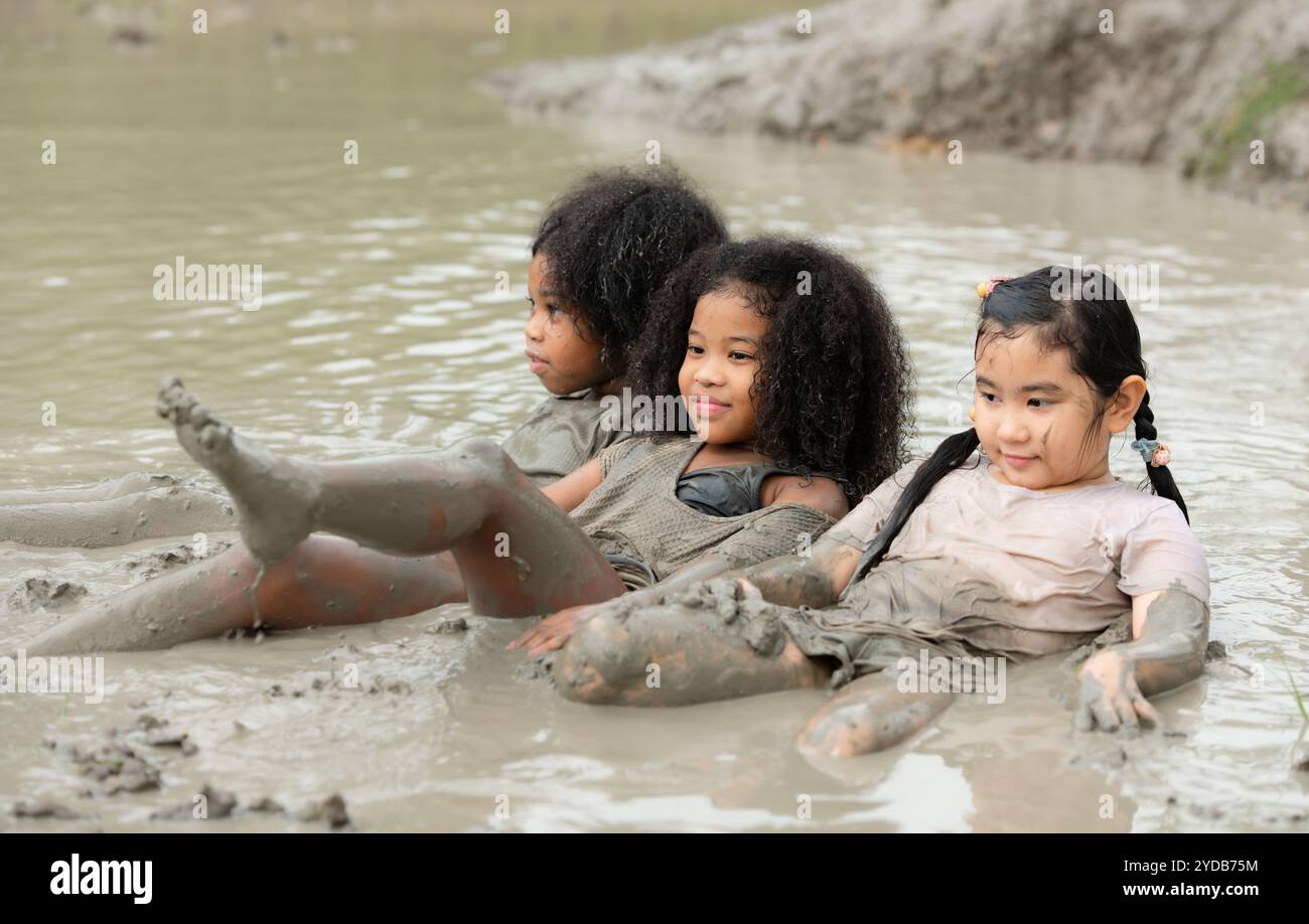 Little girls have fun playing in the mud in the community fields. with parents watching from a ...
