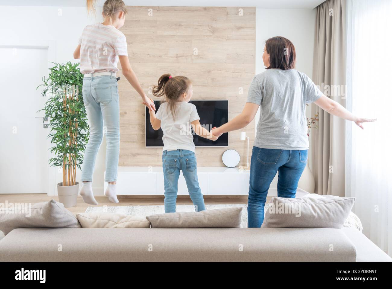 Mother and two daughters having fun jumping on a sofa in living room Stock Photo - Alamy