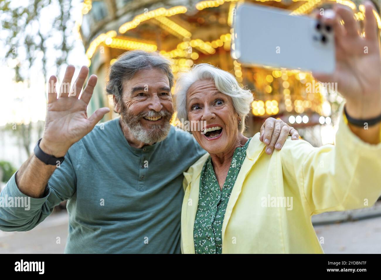 Senior couple waving at camera while taking selfie in the city next to ...