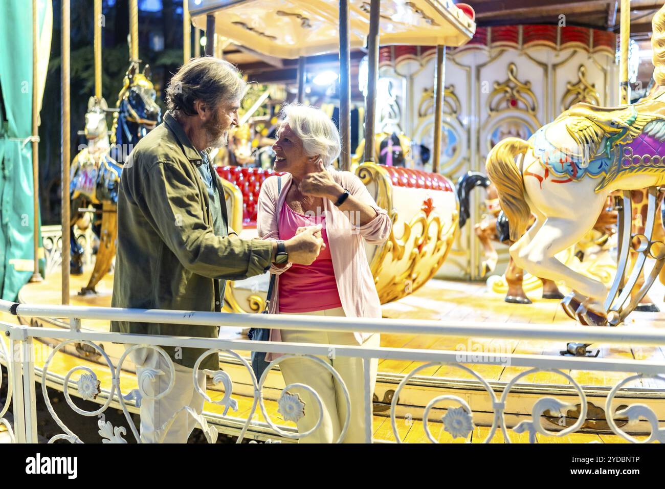 Senior man and woman enjoying ride in an old-fashion carousel standing ...