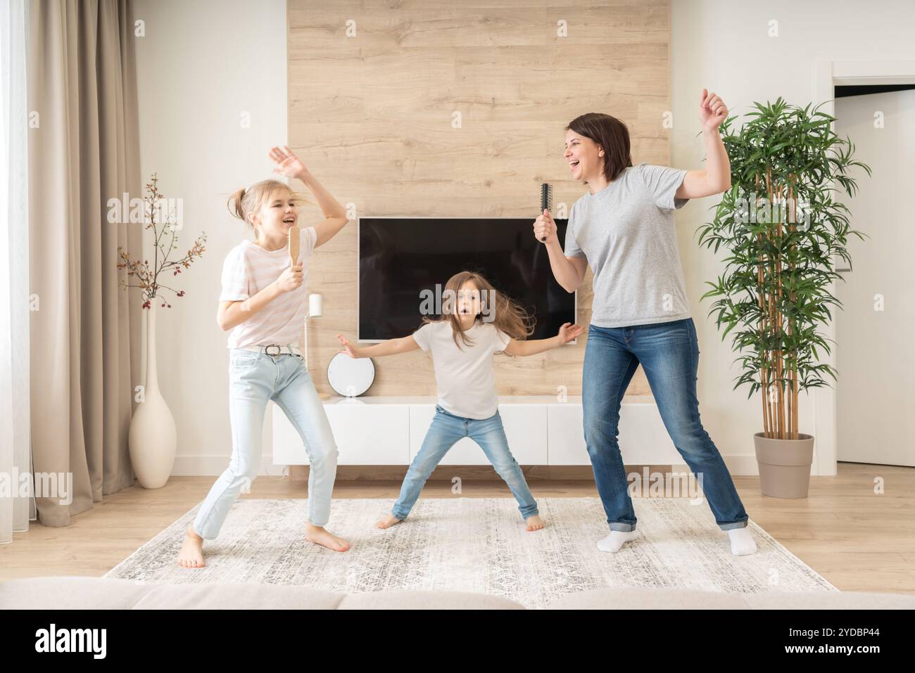 Happy mother and two daughters having fun singing karaoke song in hairbrushes. mother laughing ...