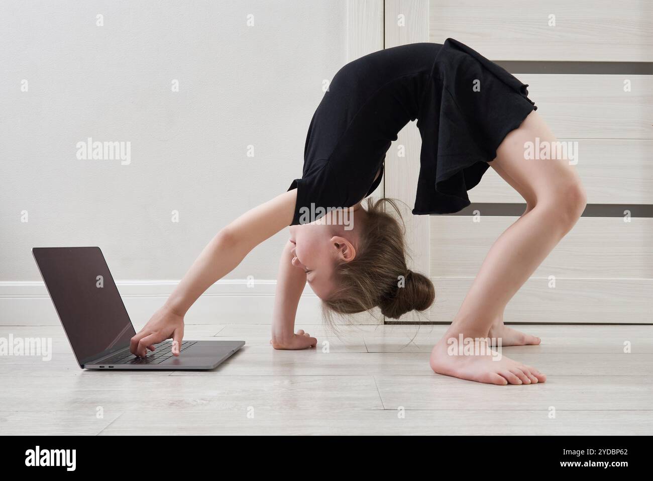 Little girl doing gymnastics exercises at home using online learning with laptop computer ...