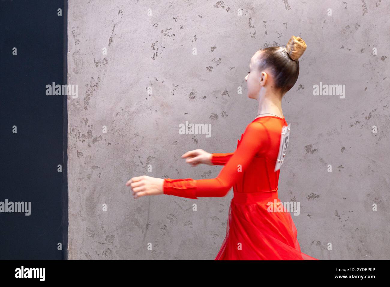 happy girl spinning back in a bright red dance dress on a gray ...