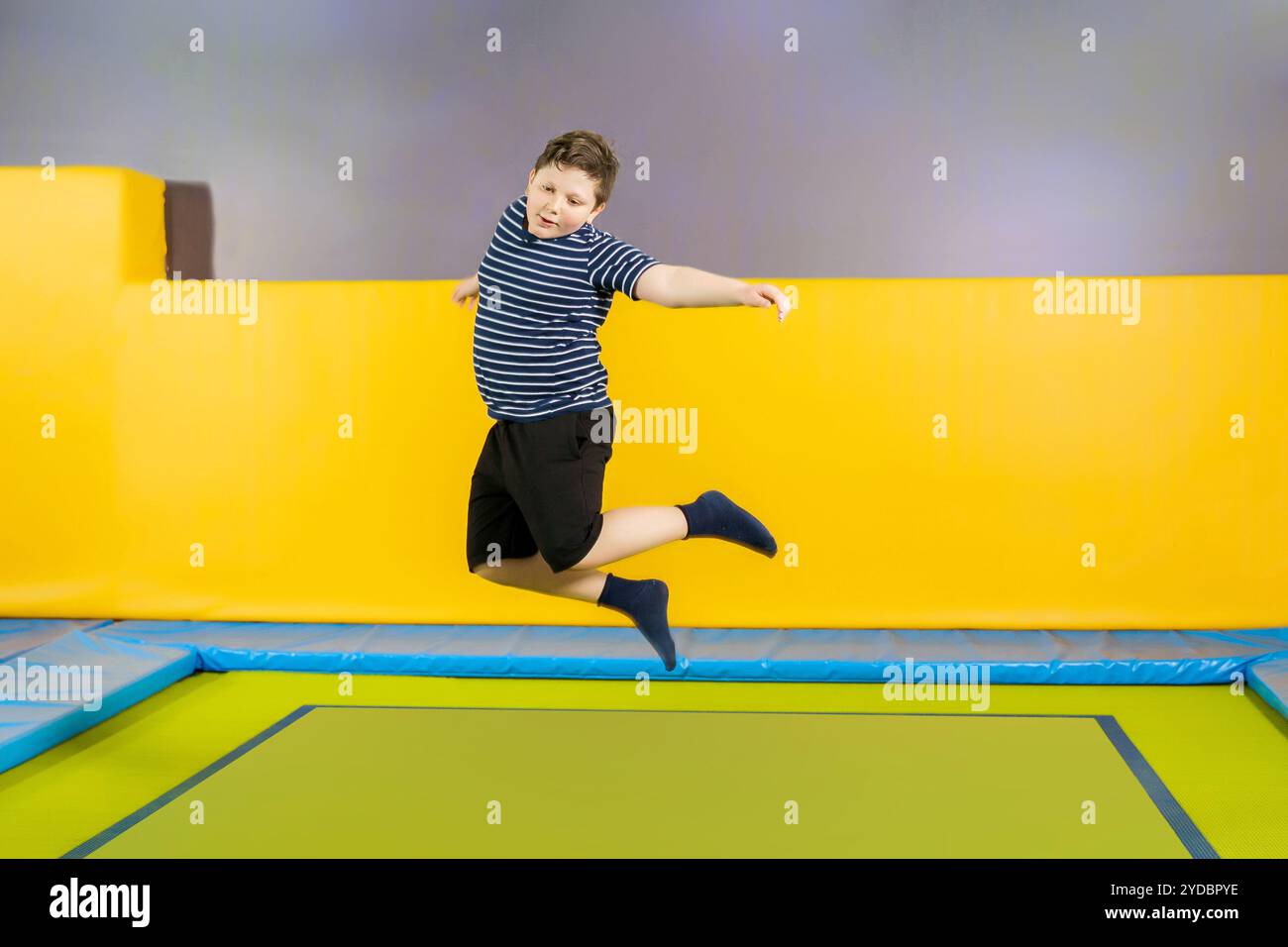 Overweight cute little boy jumping on trampoline indoors in a sport ...