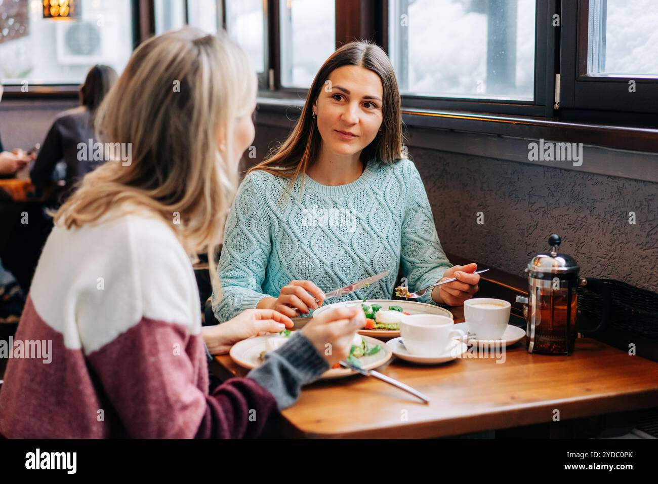 Two pretty young women talking while sitting and eating in a restaurant on a winter day Stock ...
